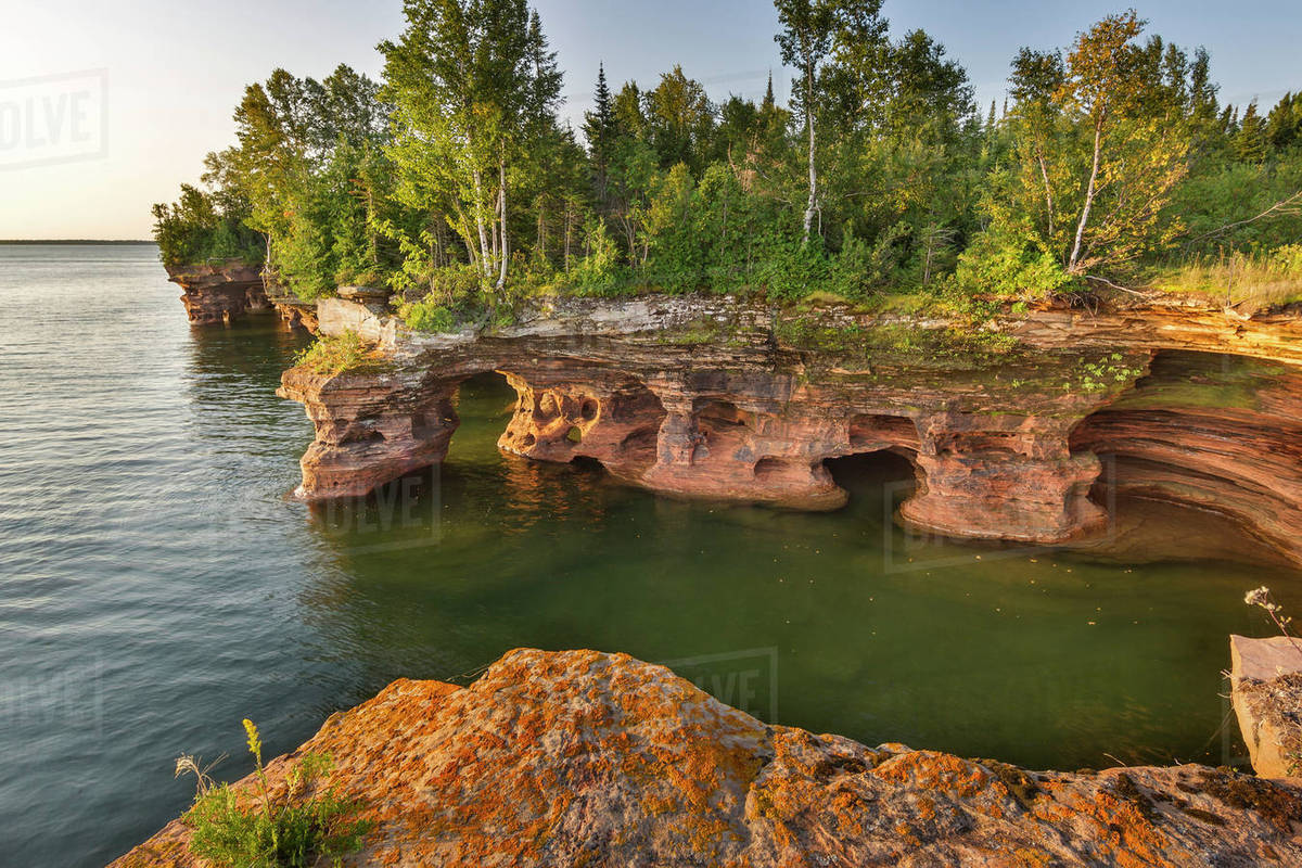 Layered sandstone cliffs and sea caves at sunrise on Devils Island in ...