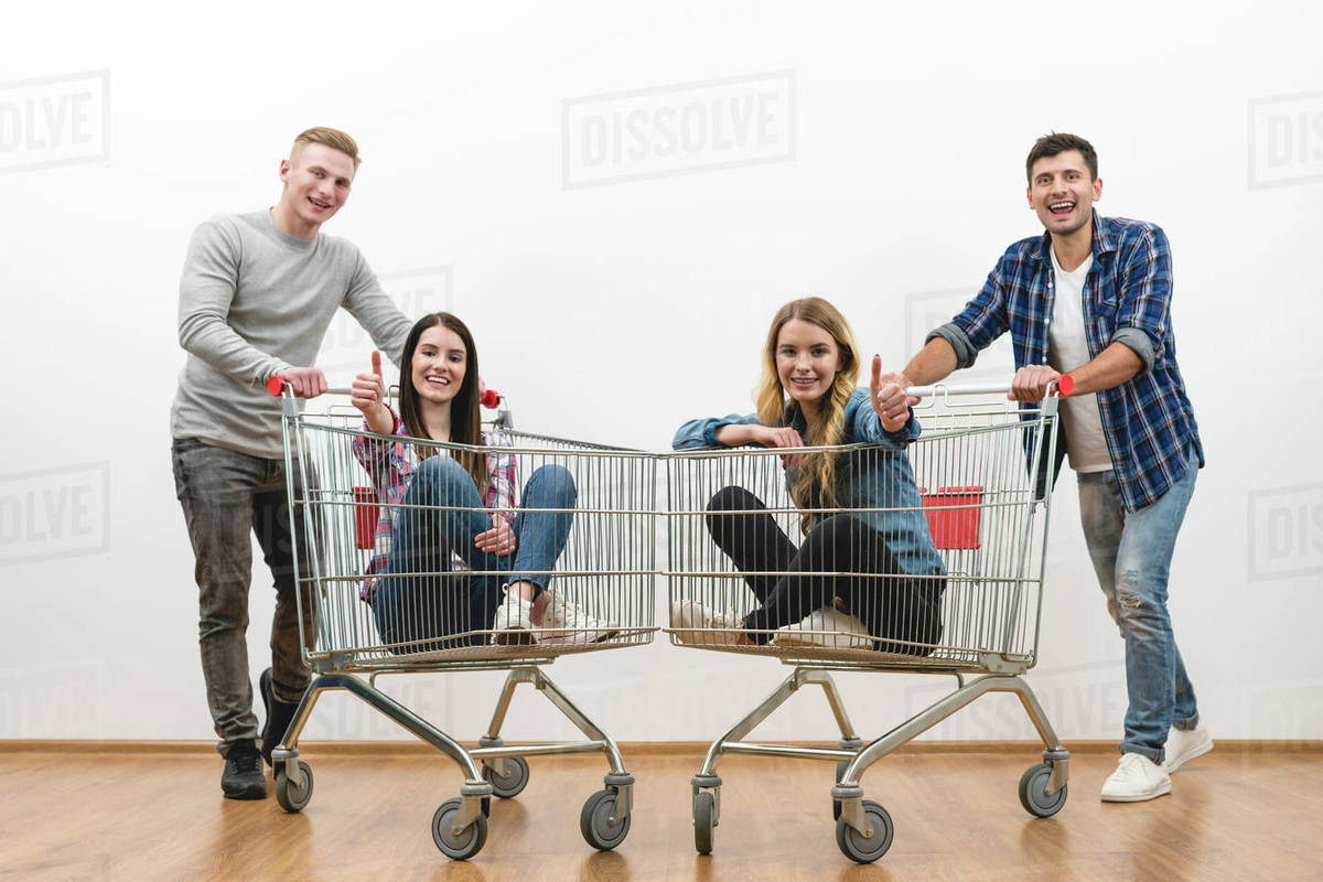 The four positive people fun with a shopping cart on a white wall ...