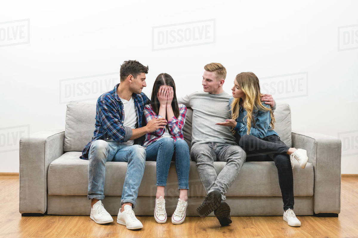 The four happy friends sit on the sofa on a white wall background ...