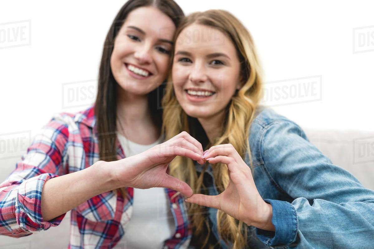 The two happy girls show the heart symbol on the white background ...