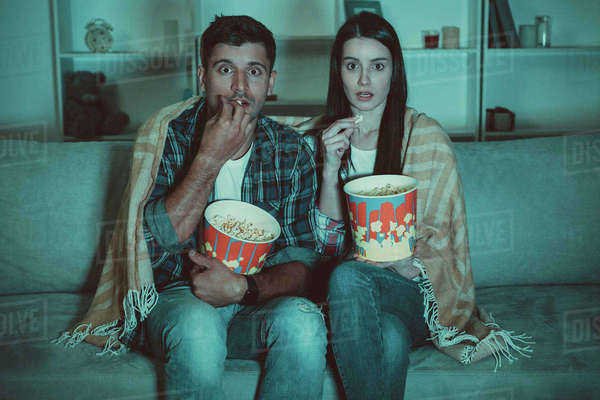 The couple eating popcorn and watch a horror movie on the sofa ...