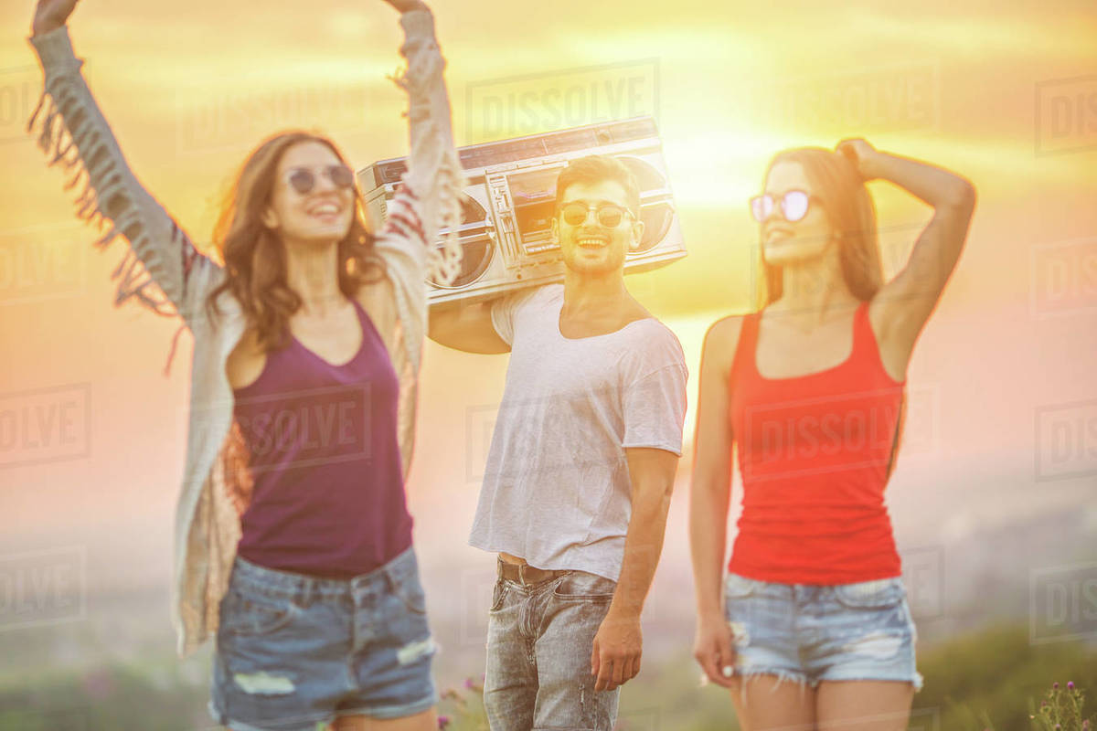 The happy people with a boom box fun in the background of the sunset ...