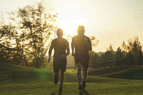 The happy men running on the park grass on the sunset background ...