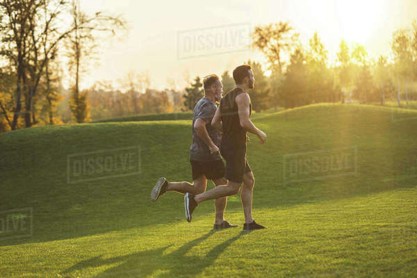 The two men running on the grass in the park on the sunrise background ...
