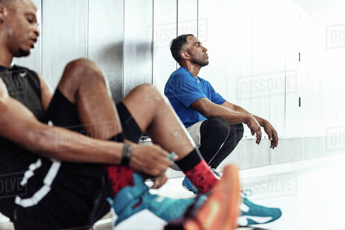 Exhausted male basketball players taking a break on changing room floor ...