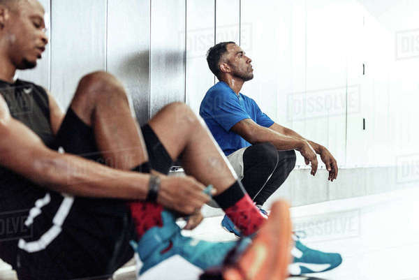 Exhausted male basketball players taking a break on changing room floor ...