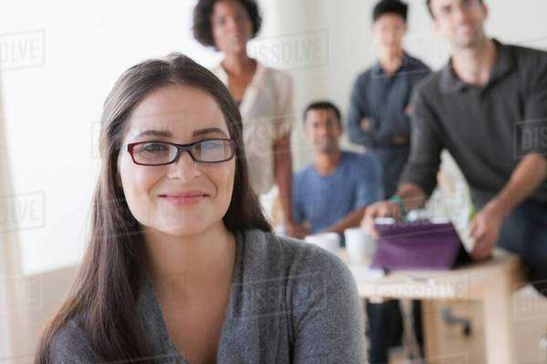 Portrait of young female office worker in front of colleagues - Stock ...