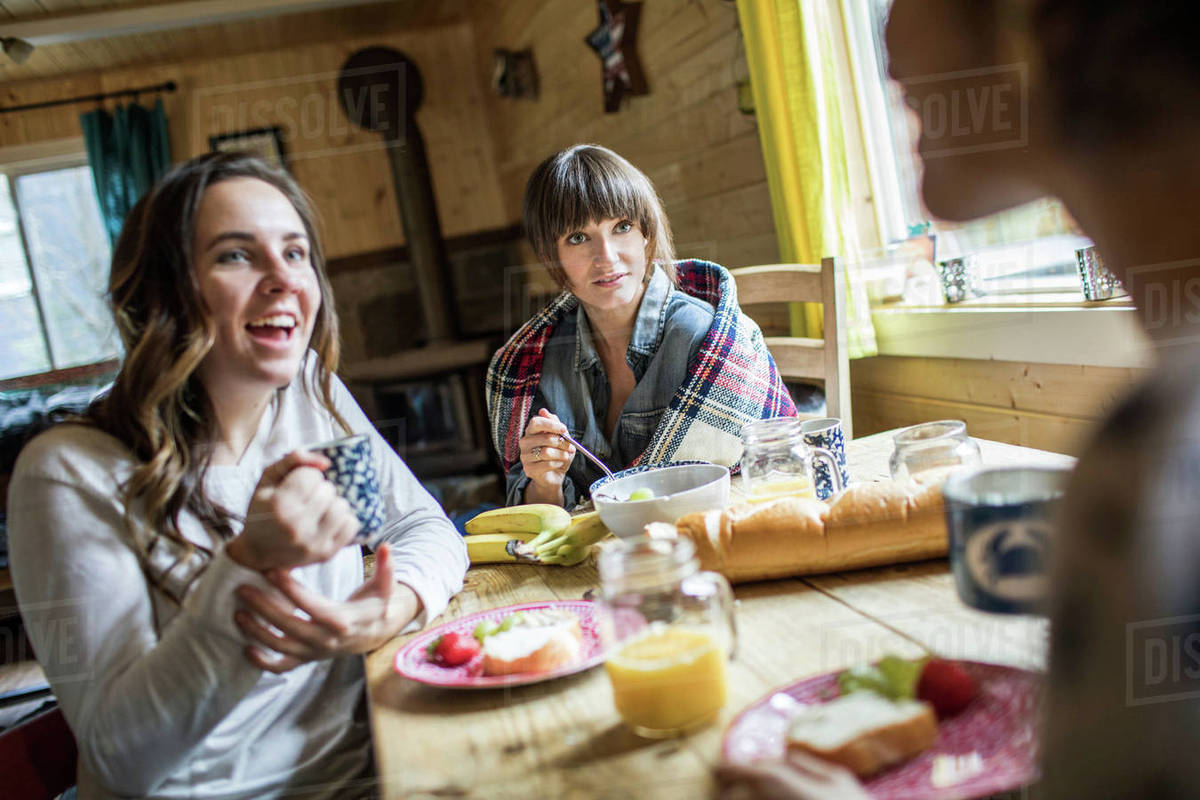 Three friends sitting around table, eating breakfast - Royalty-free ...
