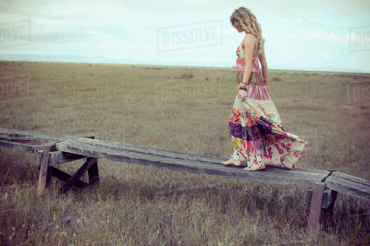 Young woman in boho maxi dress walking on elevated wooden walkway in ...