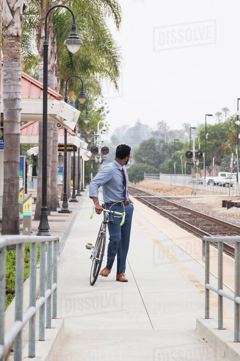 Young businessman cyclist looking back from rail station platform ...