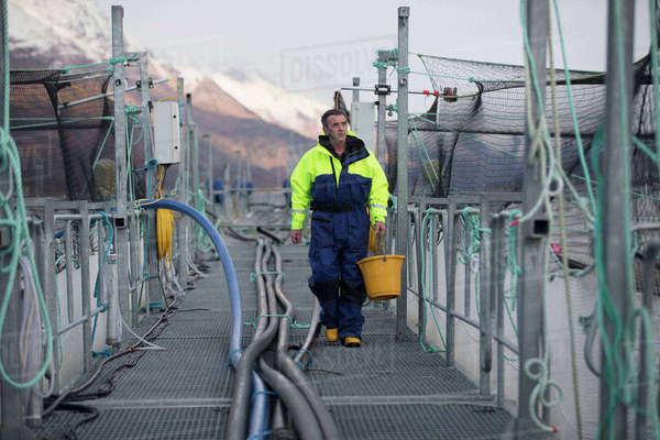 Worker on salmon farm in rural lake - Stock Photo - Dissolve