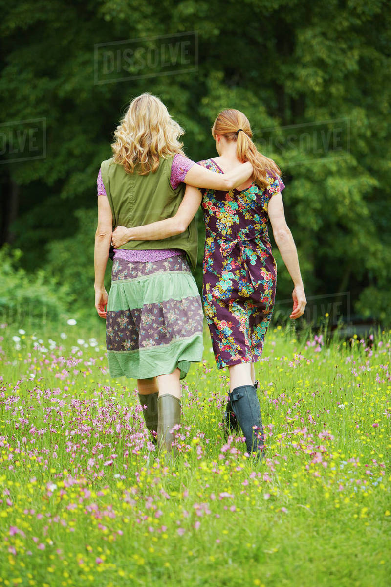Rear view of two women walking in wildflower meadow - Royalty-free ...