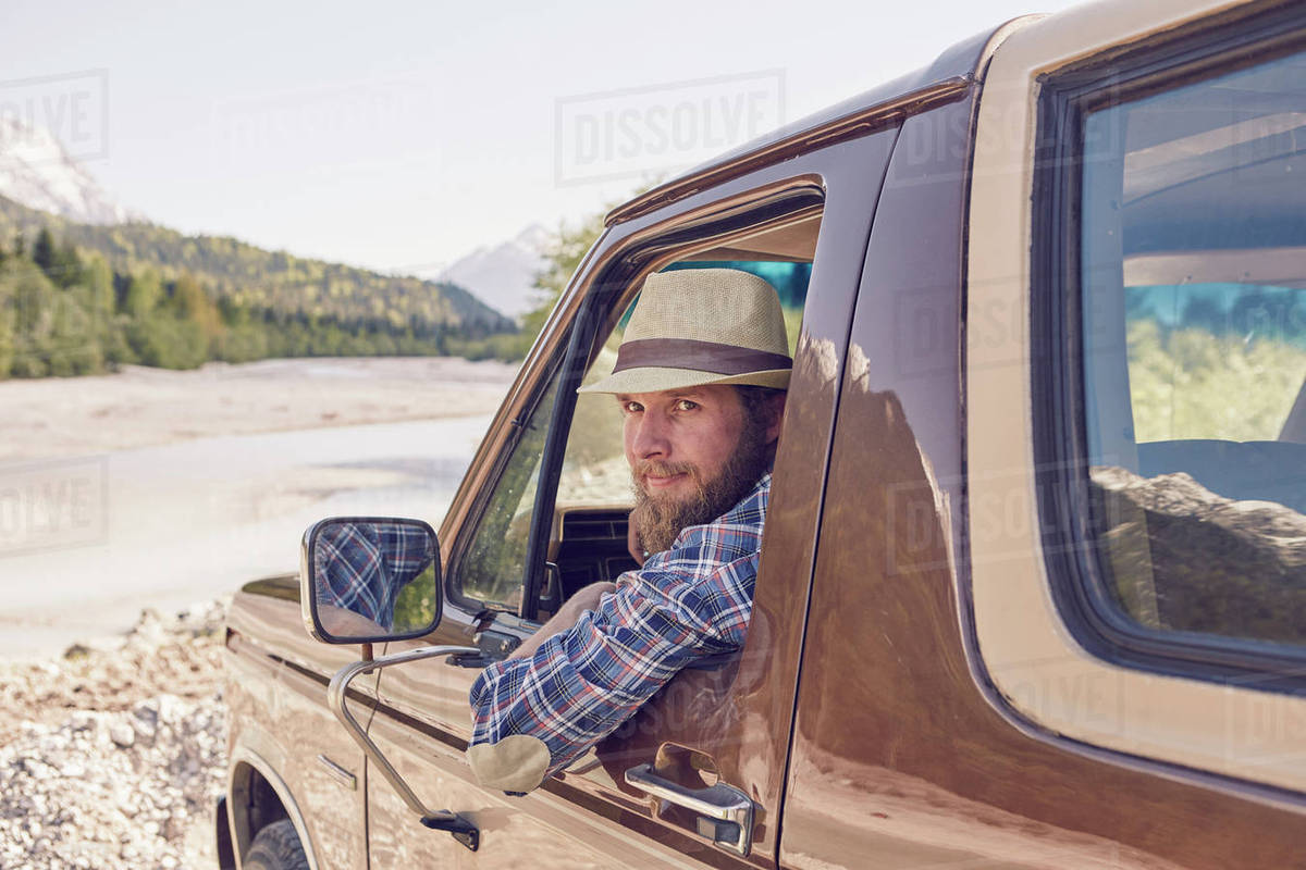 Mid adult man sitting in truck, leaning out window, looking at camera ...