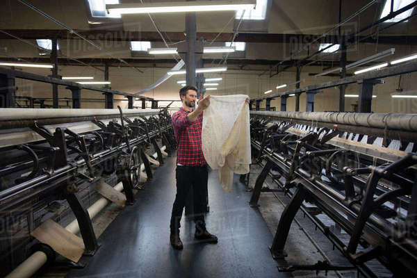 Portrait of male weaver examining cloth from old weaving machine in ...