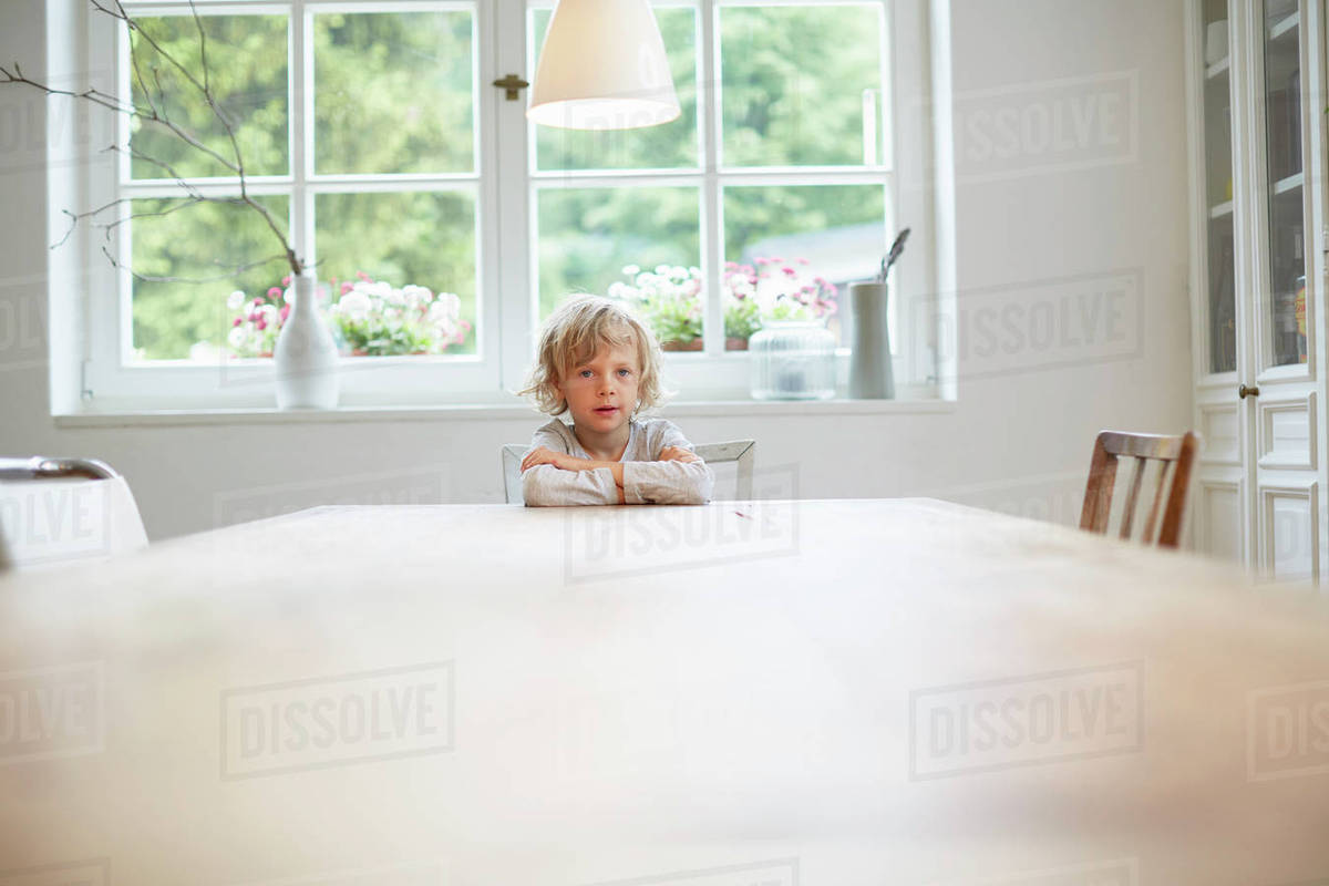 Portrait of young boy sitting at empty dining table - Stock Photo ...