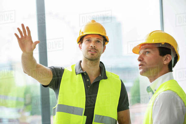 Two men wearing hi vis vest, having discussion in newly constructed ...