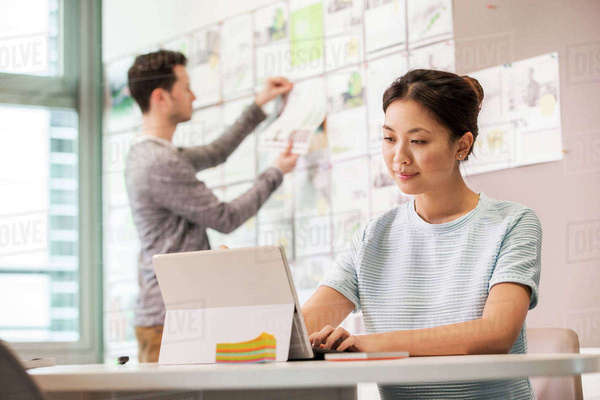 Female digital designer typing on laptop and colleague arranging mood ...