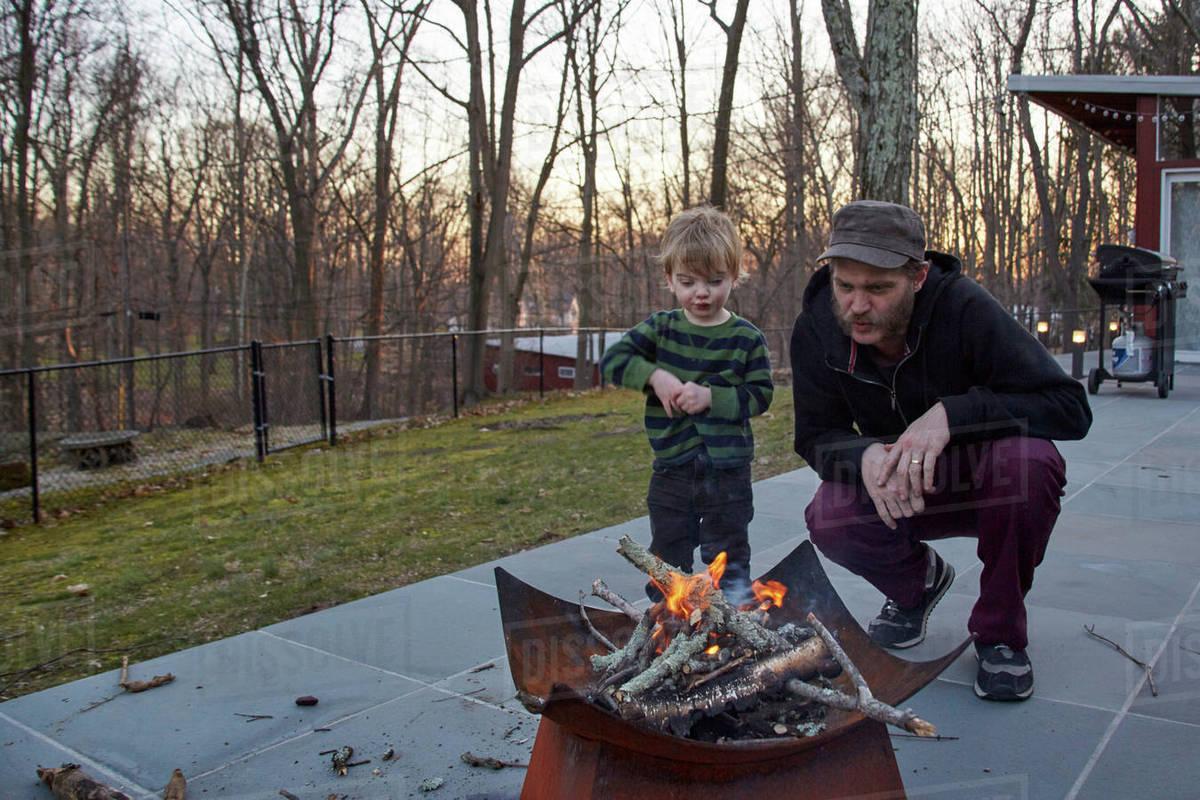 Boy and father tending fire in patio fire pit - Royalty-free Stock ...