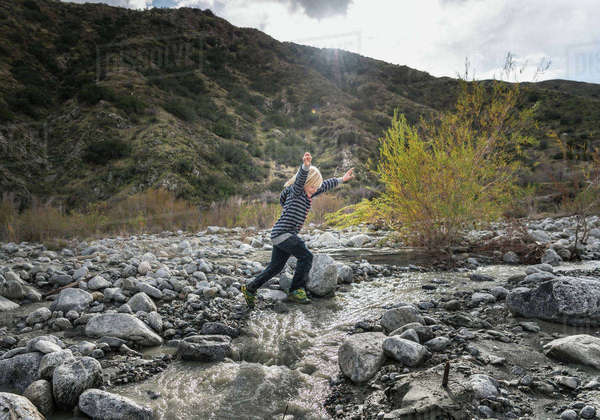 Boy leaping over rocks on riverbed - Royalty-free Stock Photo | Dissolve
