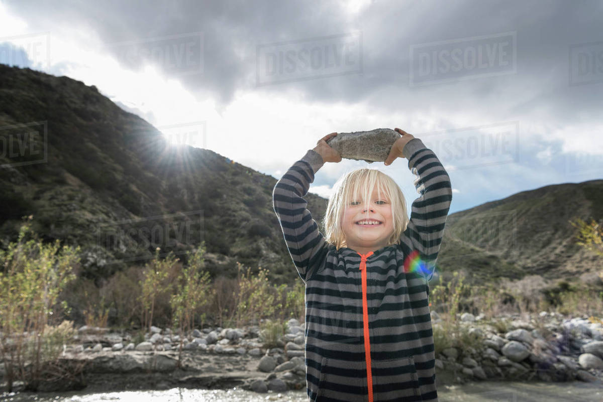 Portrait of cute boy holding up rock from riverbed - Stock Photo - Dissolve