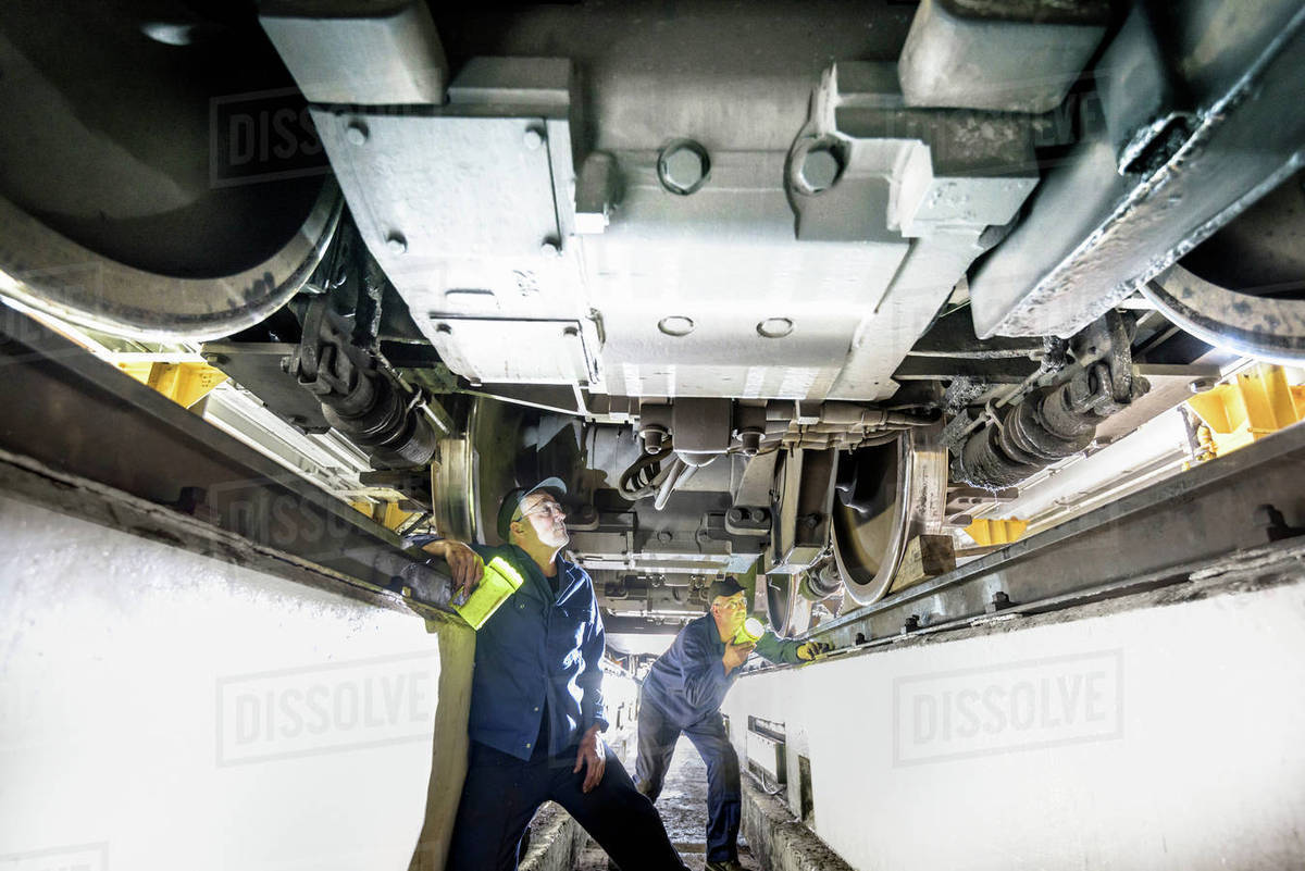 Locomotive engineers inspecting underside of locomotive in train works ...