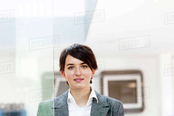 Portrait of young female sales manager by glass door in office ...