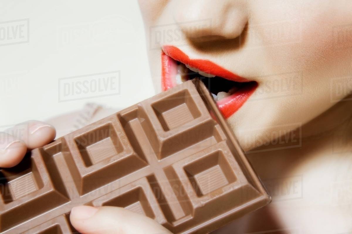 Young woman biting chocolate, close up - Stock Photo - Dissolve