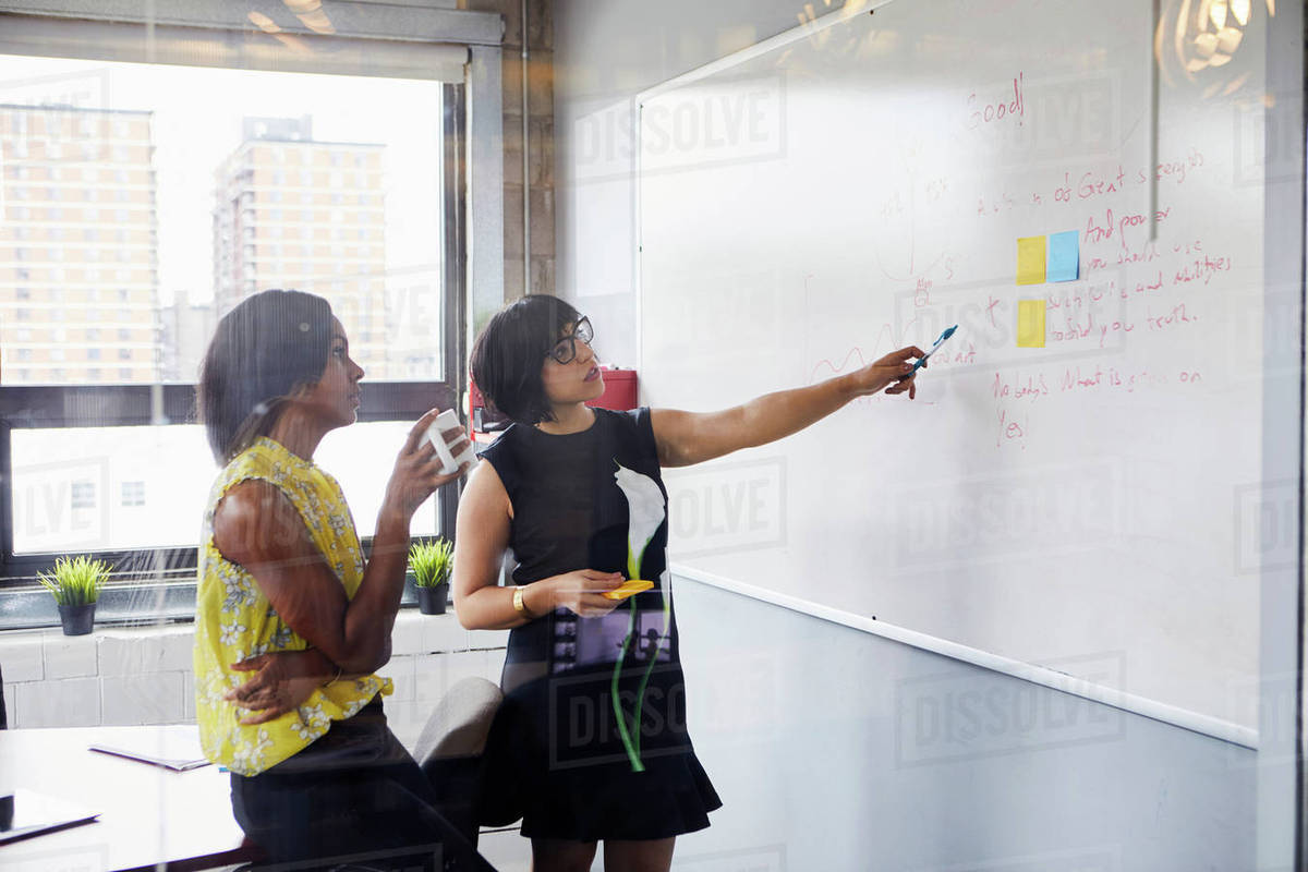Two women in office, solving problem, using whiteboard, sticky notes ...