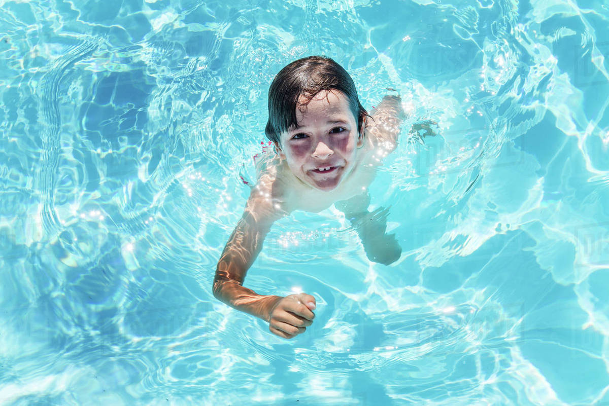 Overhead portrait of boy treading water in outdoor sunlit swimming pool ...