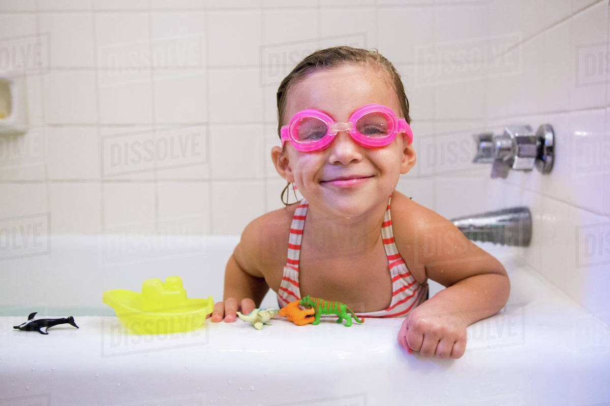 Portrait of girl wearing swimming goggles in bath, looking at camera ...