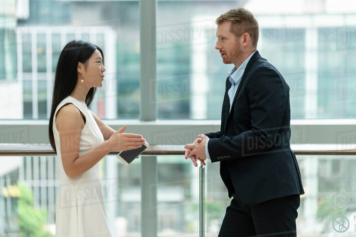 Businessman and businesswoman standing beside window, in conversation ...