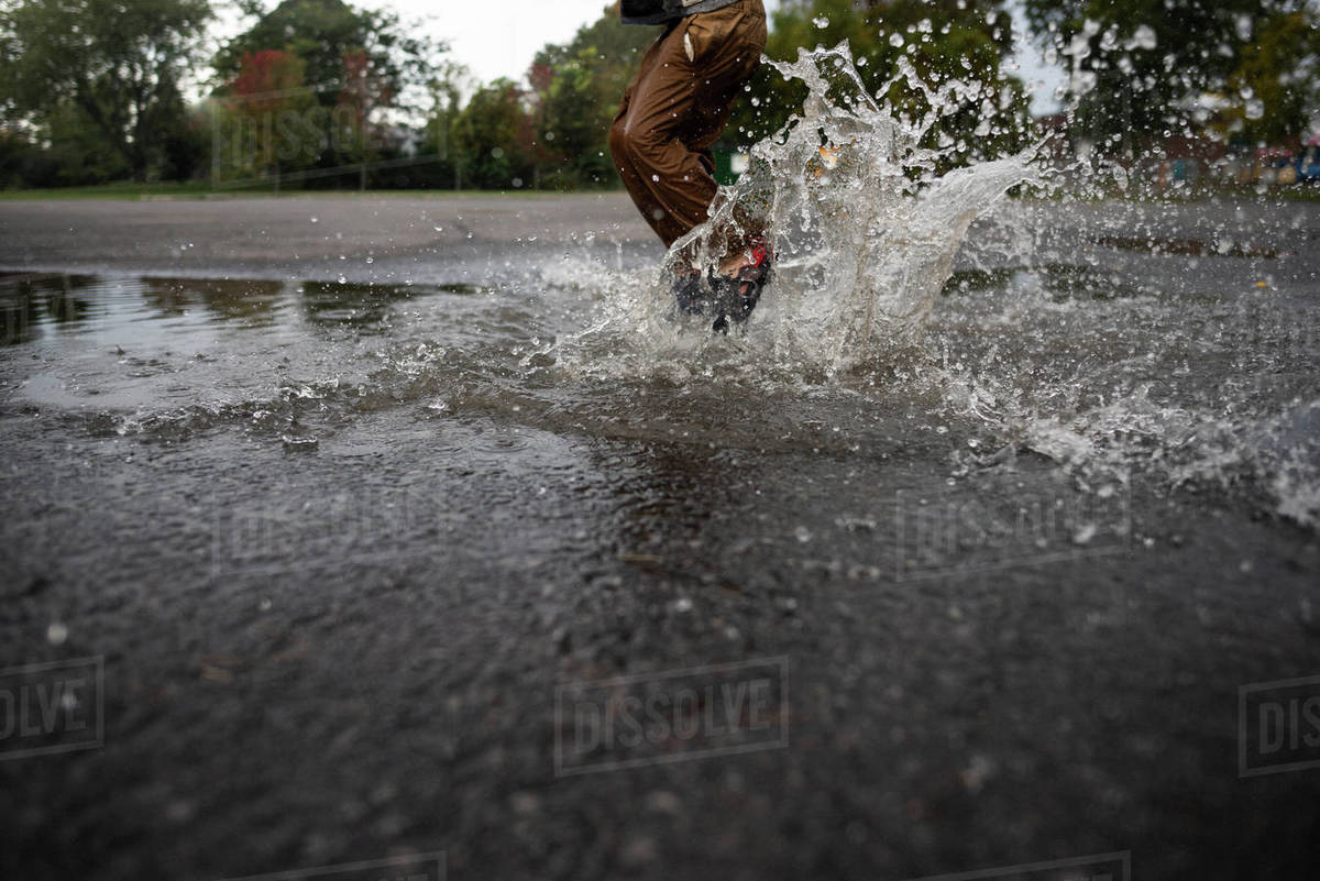 Child splashing in puddle on road - Royalty-free Stock Photo | Dissolve
