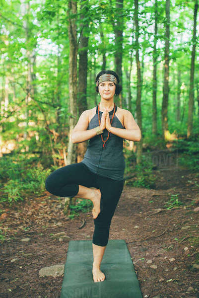Woman doing tree pose in forest - Stock Photo - Dissolve