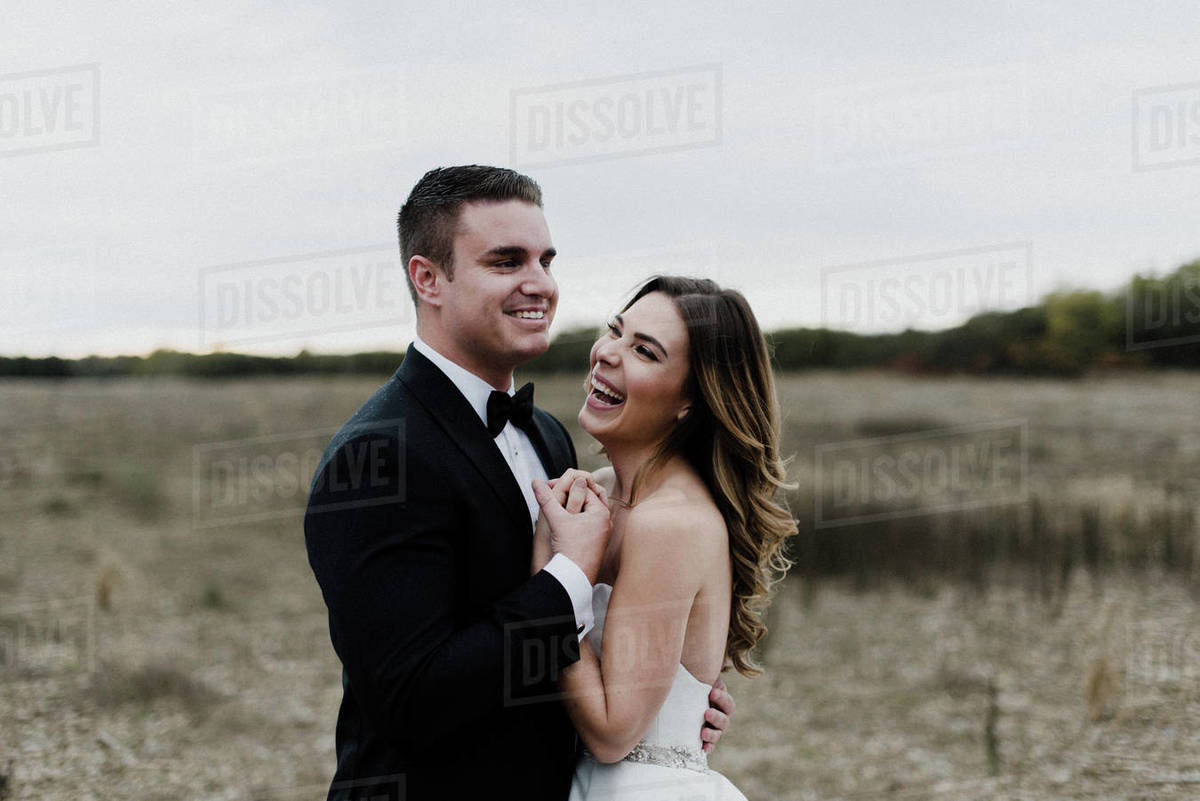 Happy young bride and groom hugging and laughing in field - Stock Photo ...