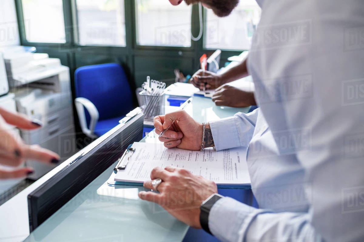 Patients completing forms with help from nurse at hospital reception ...