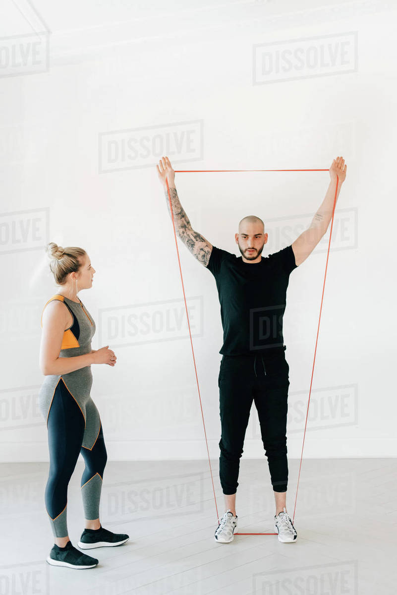 Woman observing fitness instructor using resistance band in studio ...