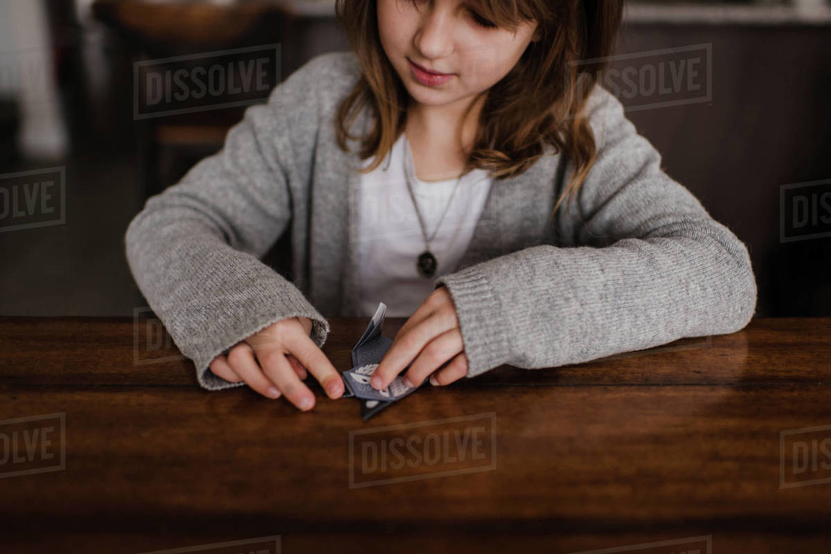 Girl at table folding paper, doing origami, head and shoulders - Stock ...