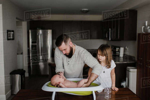 Young man bathing baby son while daughter watches in kitchen - Royalty ...