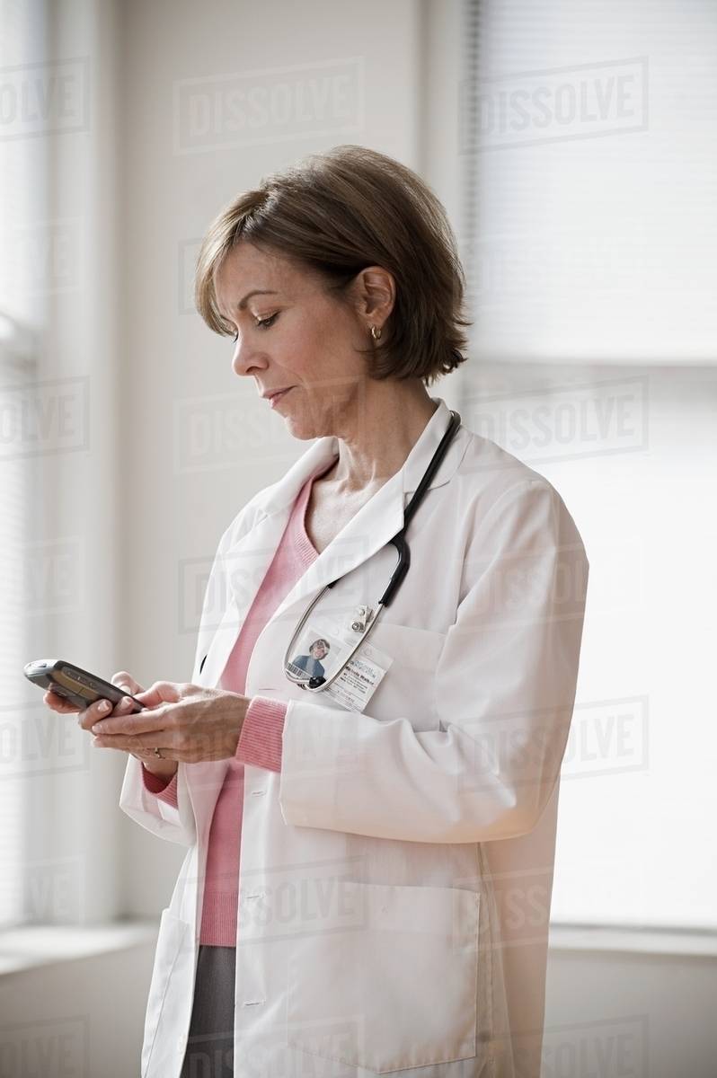 Doctor looking at cellphone - Royalty-free Stock Photo | Dissolve