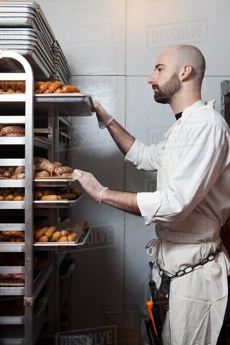 Butcher with racks of sausages on trays - Stock Photo - Dissolve