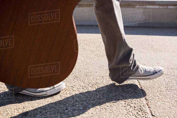 Man carrying guitar, view of legs - Stock Photo - Dissolve