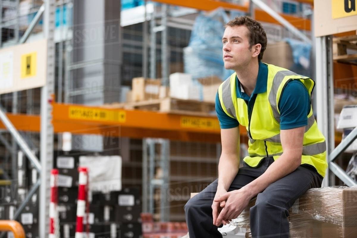 Man sitting on cardboard box in warehouse - Stock Photo - Dissolve