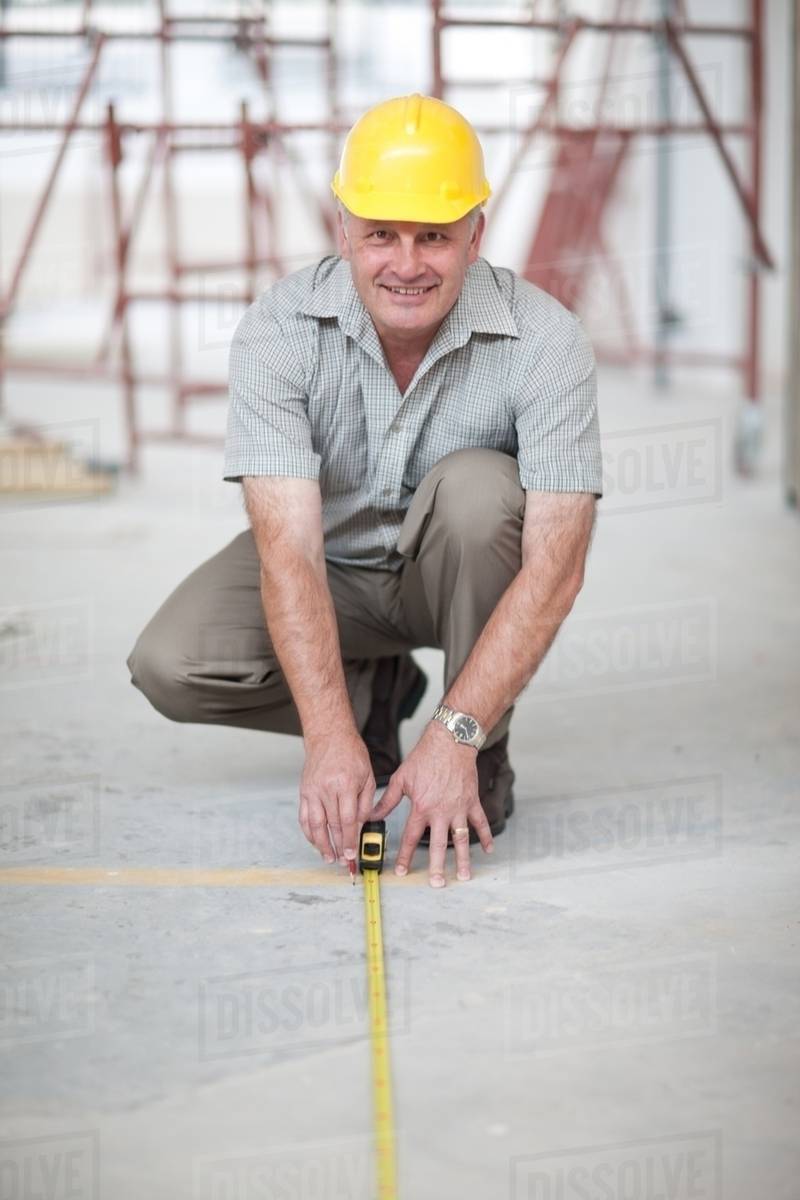 Builder measuring floor space on construction site - Stock Photo - Dissolve