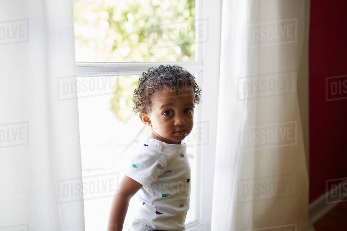 Toddler standing beside window - Stock Photo - Dissolve