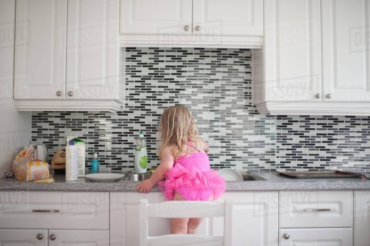 Girl standing on chair at kitchen counter - Stock Photo - Dissolve