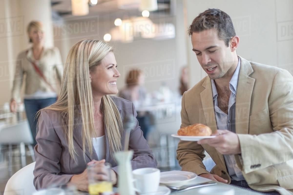 Businessman handing croissant to colleague at breakfast in hotel ...