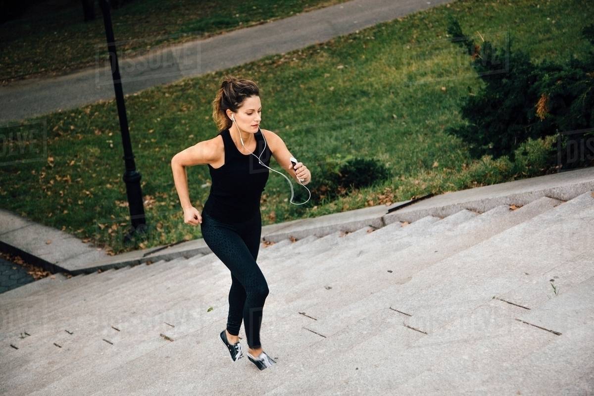 Woman running up steps in park - Royalty-free Stock Photo | Dissolve