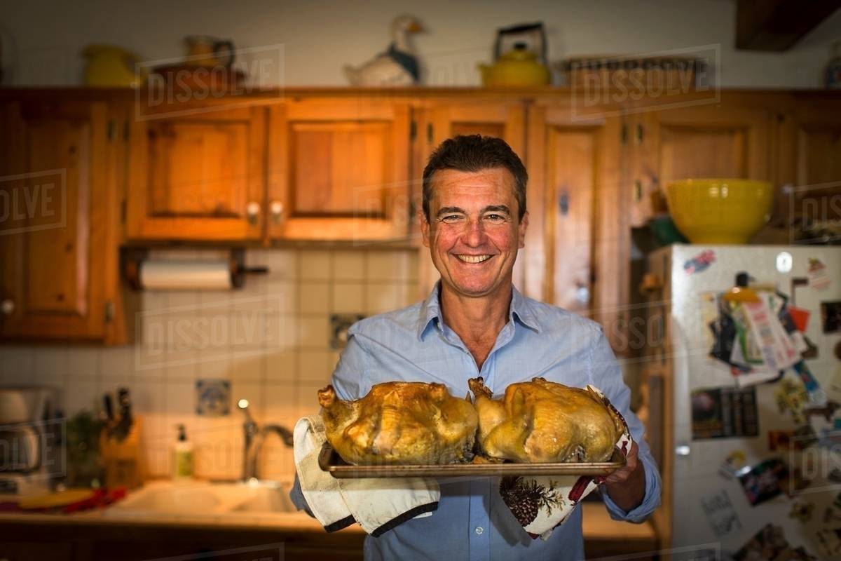 Portrait of mature man holding roast chickens in kitchen - Royalty-free ...