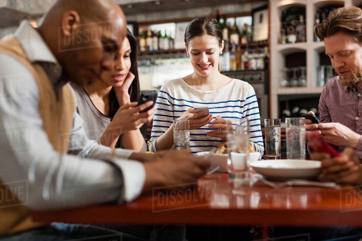 Friends at restaurant texting and showing photos using cell phones ...
