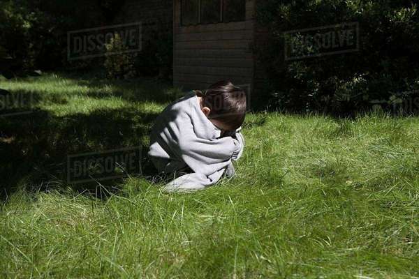 Boy cowering in a garden - Royalty-free Stock Photo | Dissolve